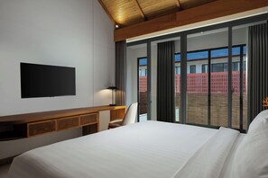 Quarto de hotel com cama, escrivaninha, cadeira, televisão e vista de um edifício por grandes janelas.
