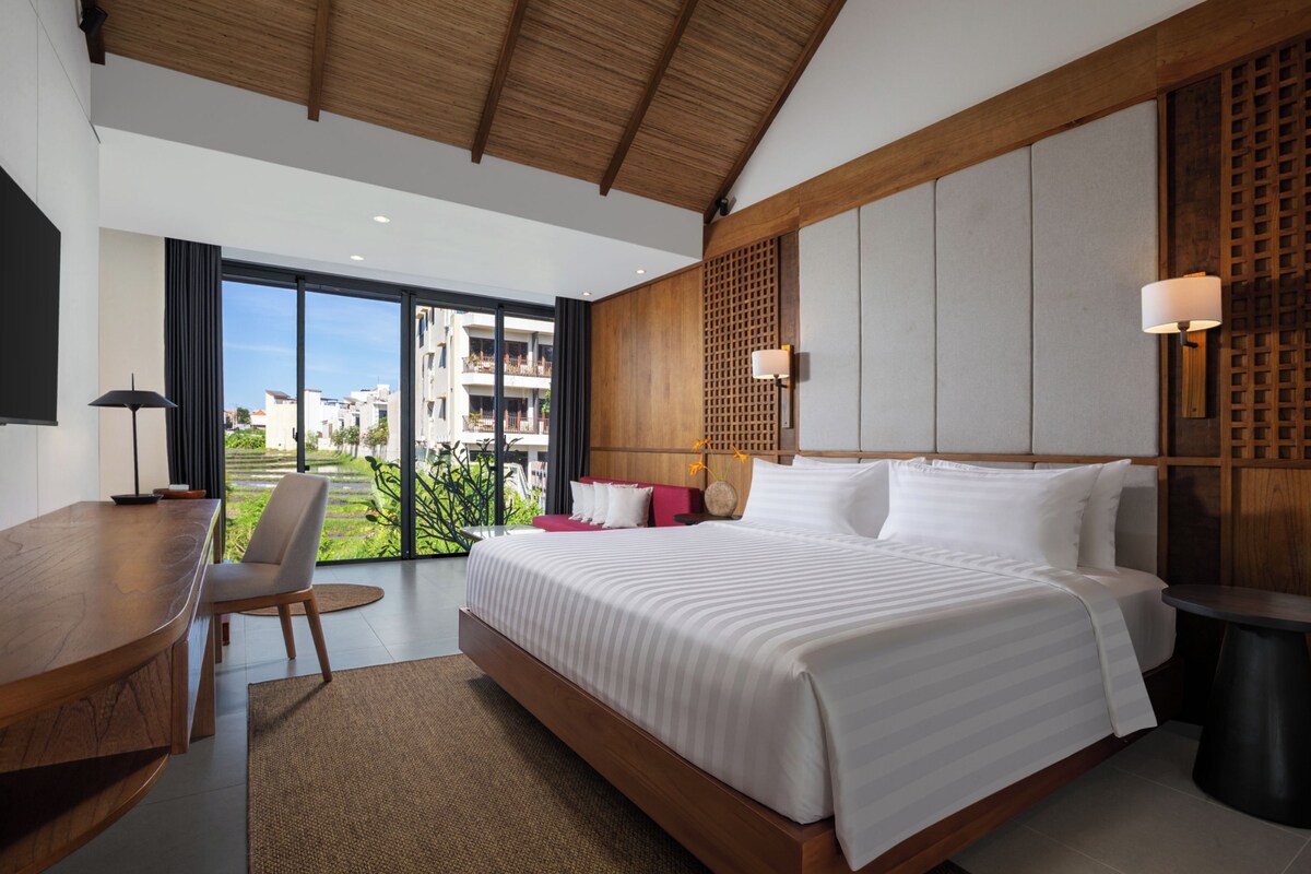 Quarto de hotel com uma cama grande, uma escrivaninha e vista para o exterior.