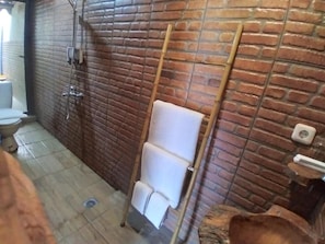 Um banheiro com parede de tijolos, toalheiro branco, chuveiro e vaso sanitário.