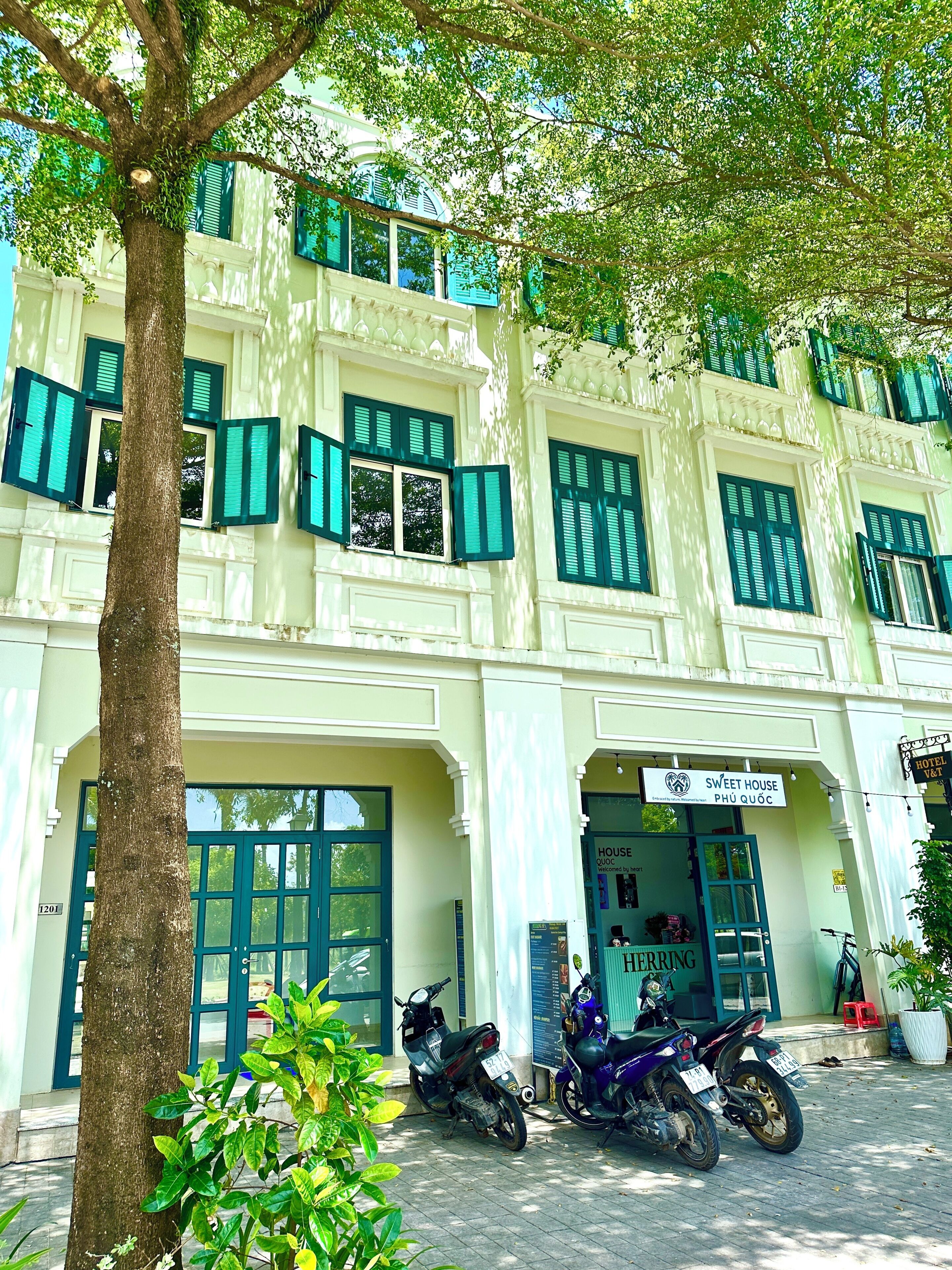 Um edifício com várias janelas e uma placa com a inscrição 'Sweet House PHU QUOC'.