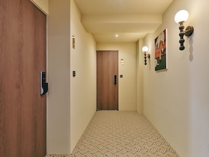 Um corredor de hotel com porta de madeira, carpete estampado, luminárias fixadas na parede e um interfone.