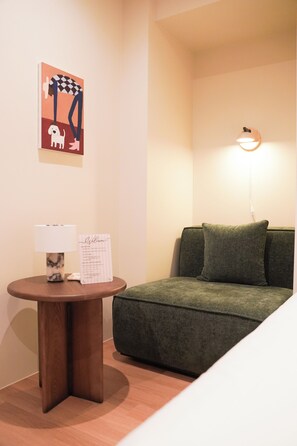 Um quarto com um sofá verde, uma mesa redonda pequena com uma luminária e uma obra de arte pendurada na parede.