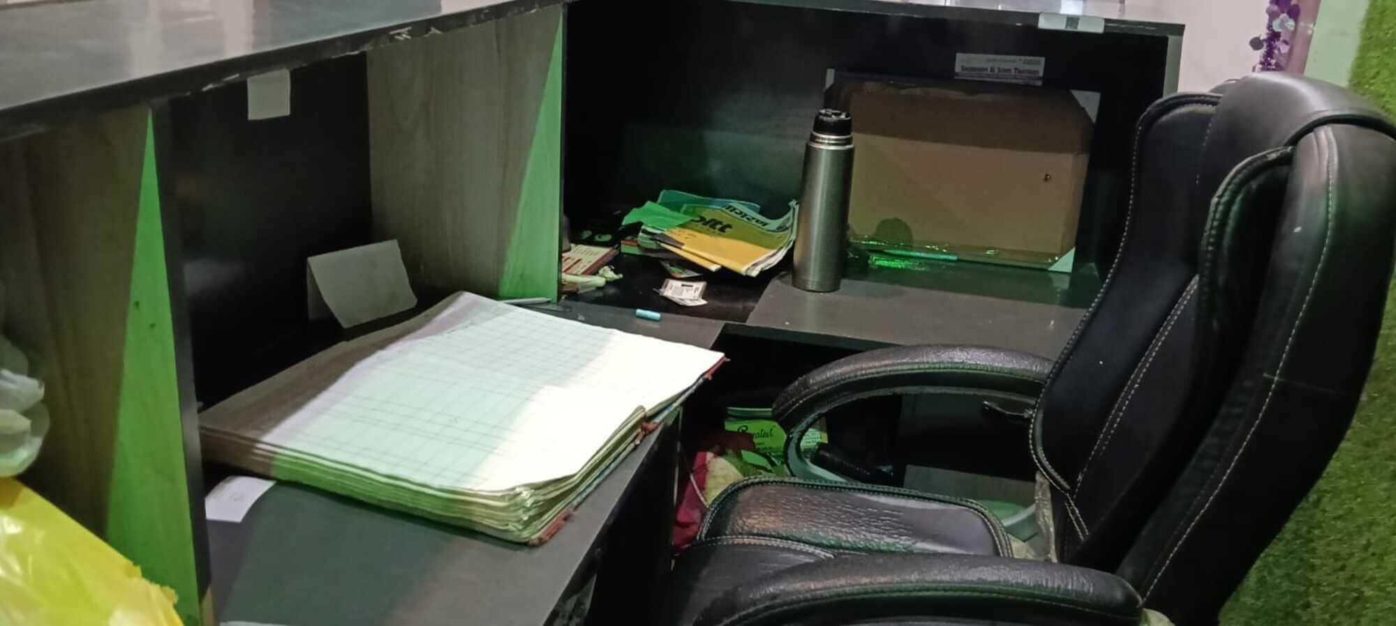 Uma escrivaninha com uma cadeira, uma pilha de papéis, uma garrafa térmica e algumas caixas.