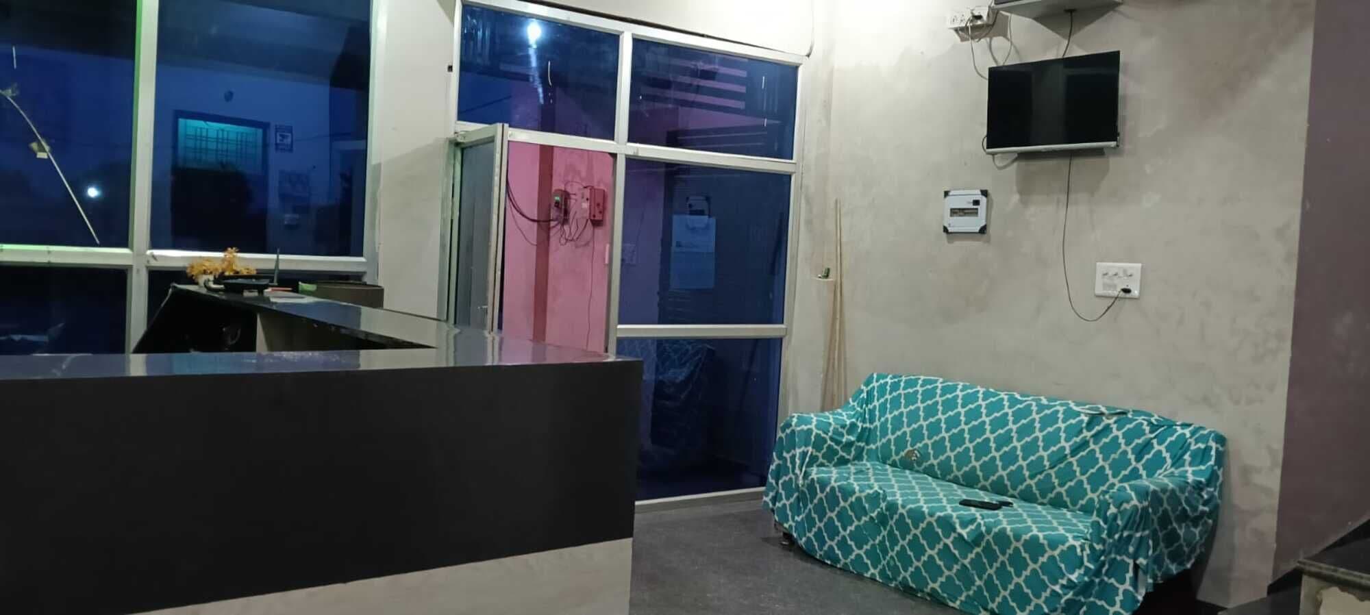 Quarto com cozinha compacta, sofá, televisão na parede e janela com cortinas.