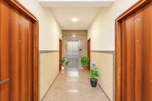 Um corredor com portas de madeira, piso de mármore e plantas em vasos.