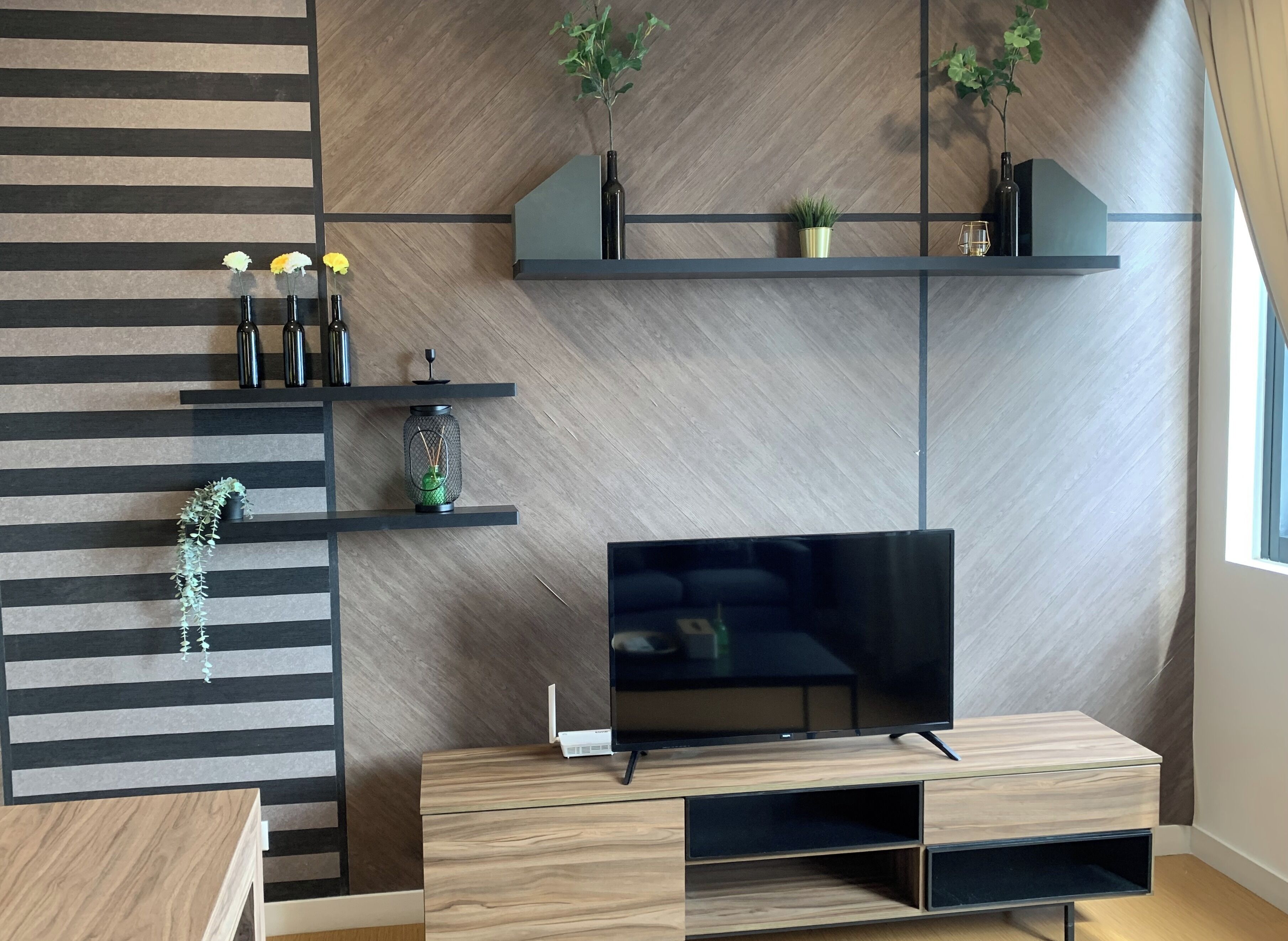 Uma sala de estar moderna com televisão de tela plana, prateleiras de madeira com objetos decorativos e uma parede listrada.