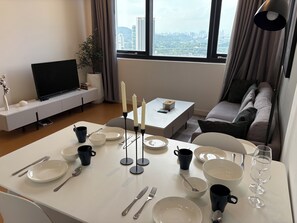 Uma sala de estar moderna com uma mesa de jantar posta para quatro pessoas, um sofá, uma televisão e vista para a cidade.