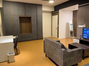 Quarto moderno com escrivaninha, sofá cinzento e televisão.