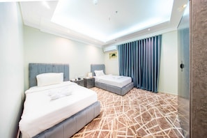 Quarto de hotel com duas camas, uma lâmpada no teto, ar condicionado, janela com cortinas e carpete estampado.