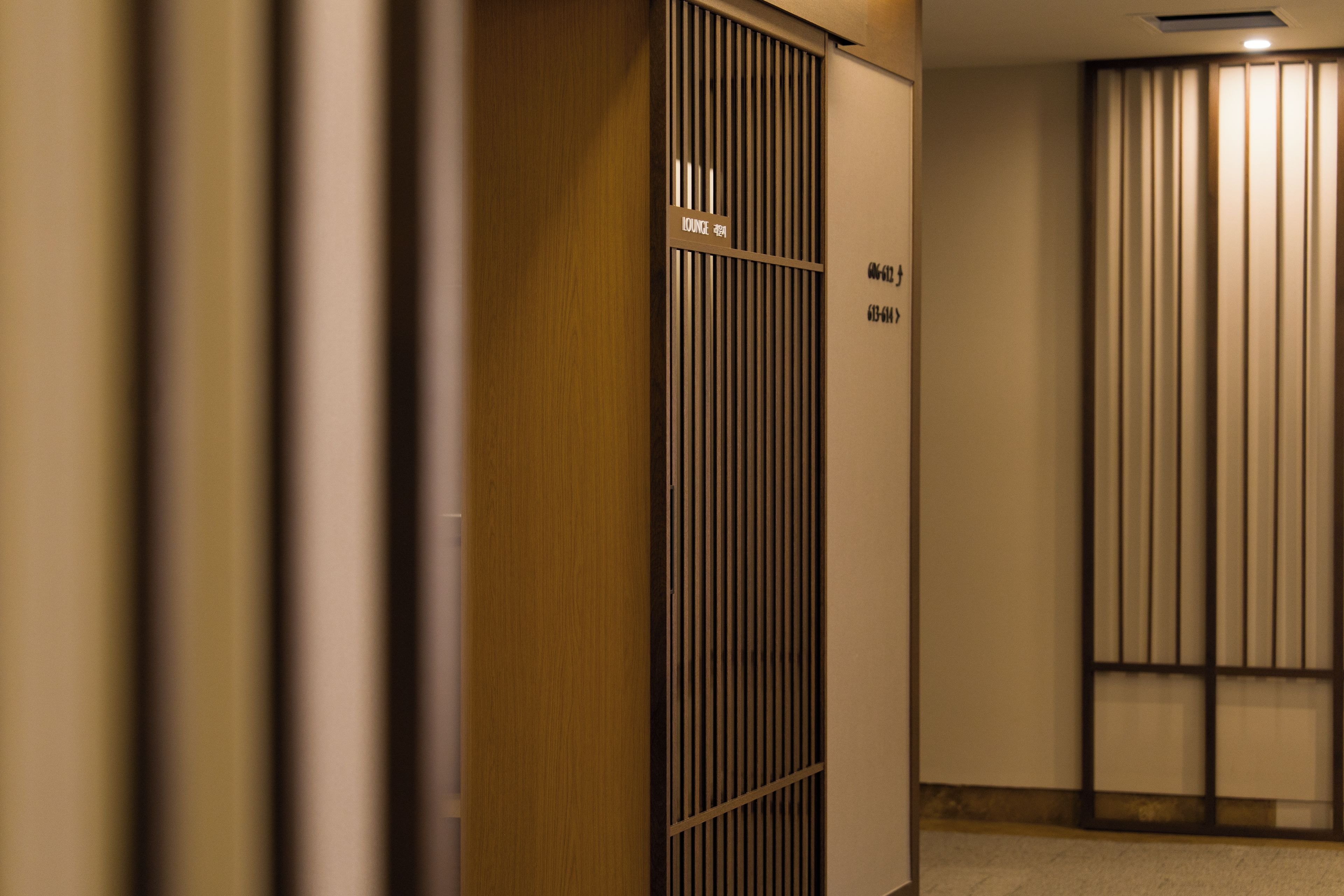 Corredor com porta de madeira identificada como 'LOUNGE' e uma grade de metal vertical.