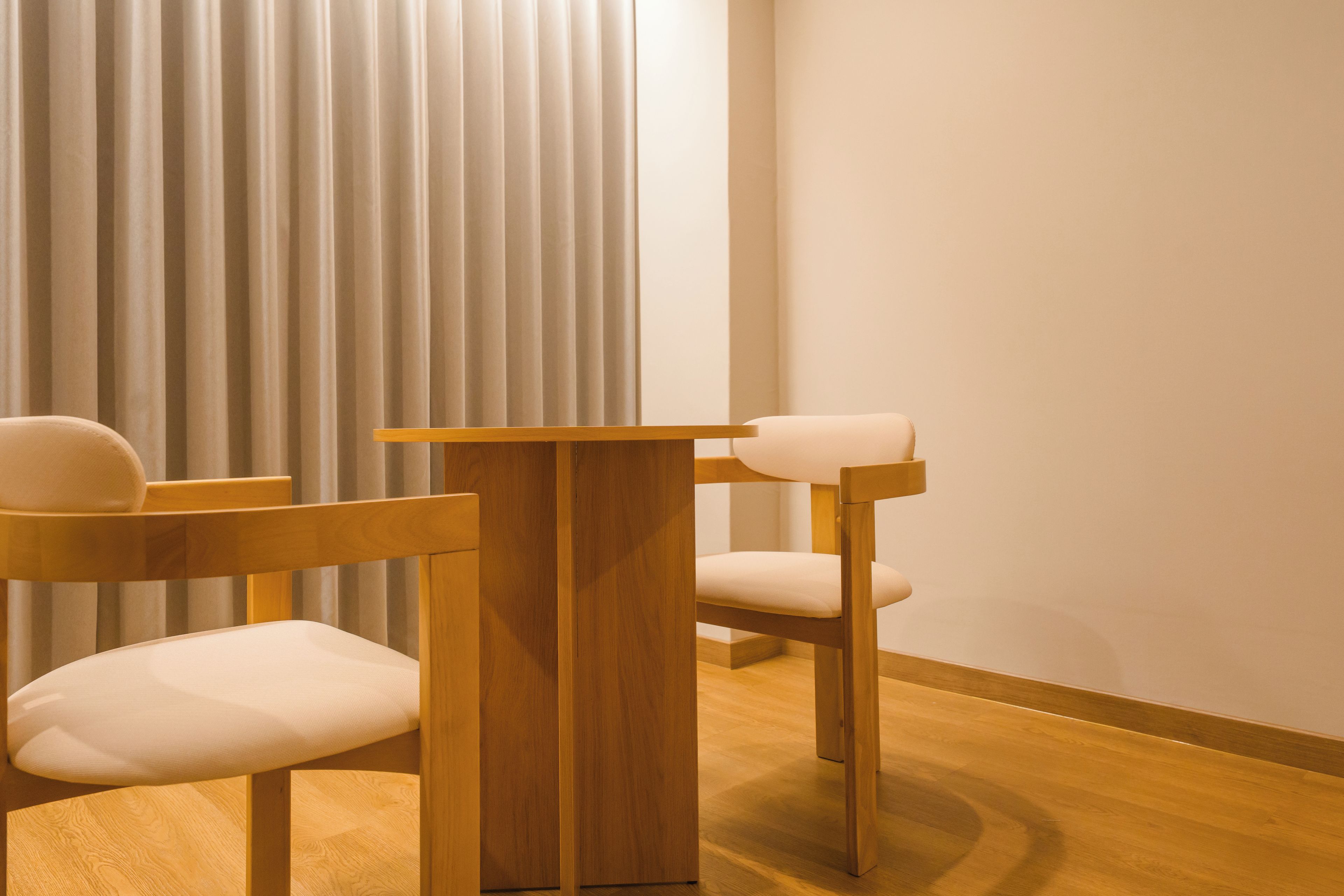 Quarto moderno com mesa de madeira e duas cadeiras, uma janela grande com persianas verticais e piso de madeira.