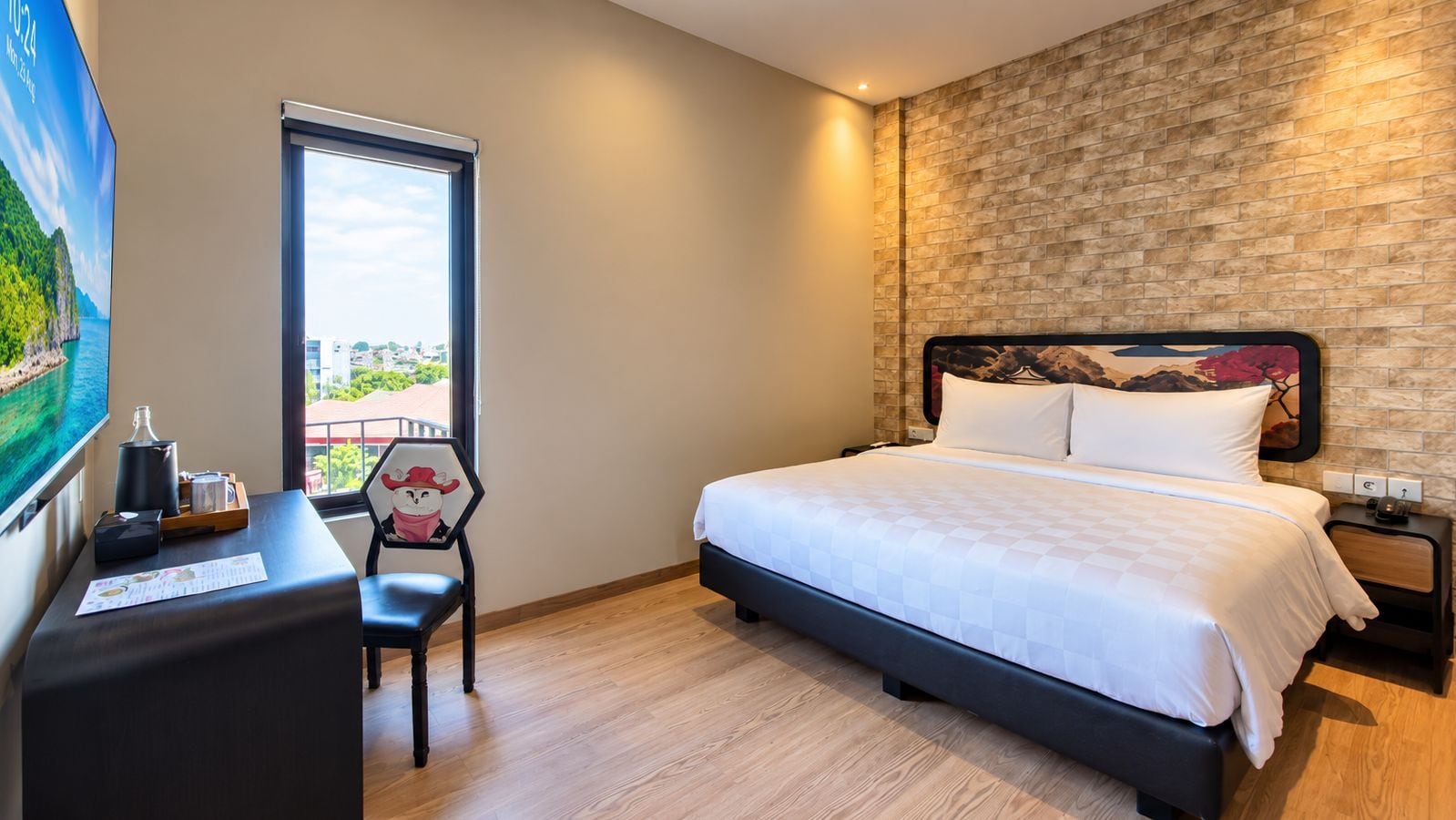Quarto de hotel com cama, escrivaninha, cadeira, janela e parede de tijolos.