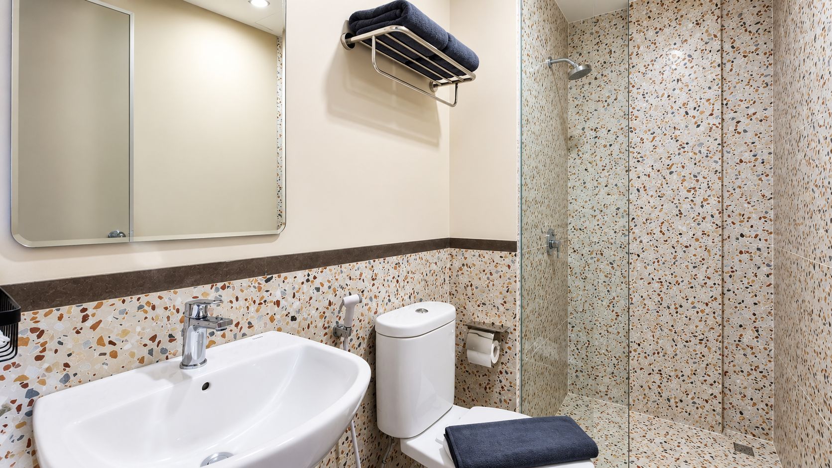 Casa de banho com lavatório branco, sanita e chuveiro com azulejos salpicados.