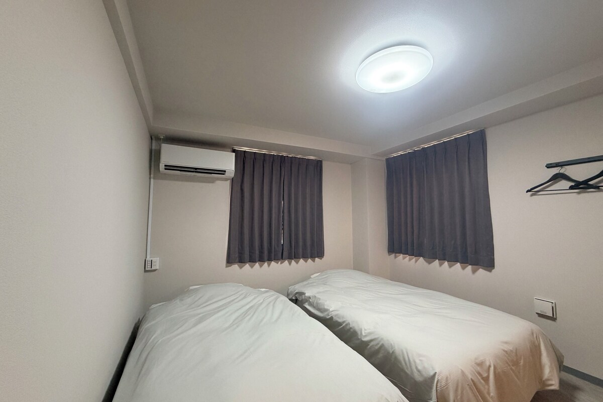 Quarto com duas camas, ar-condicionado e luminária no teto.