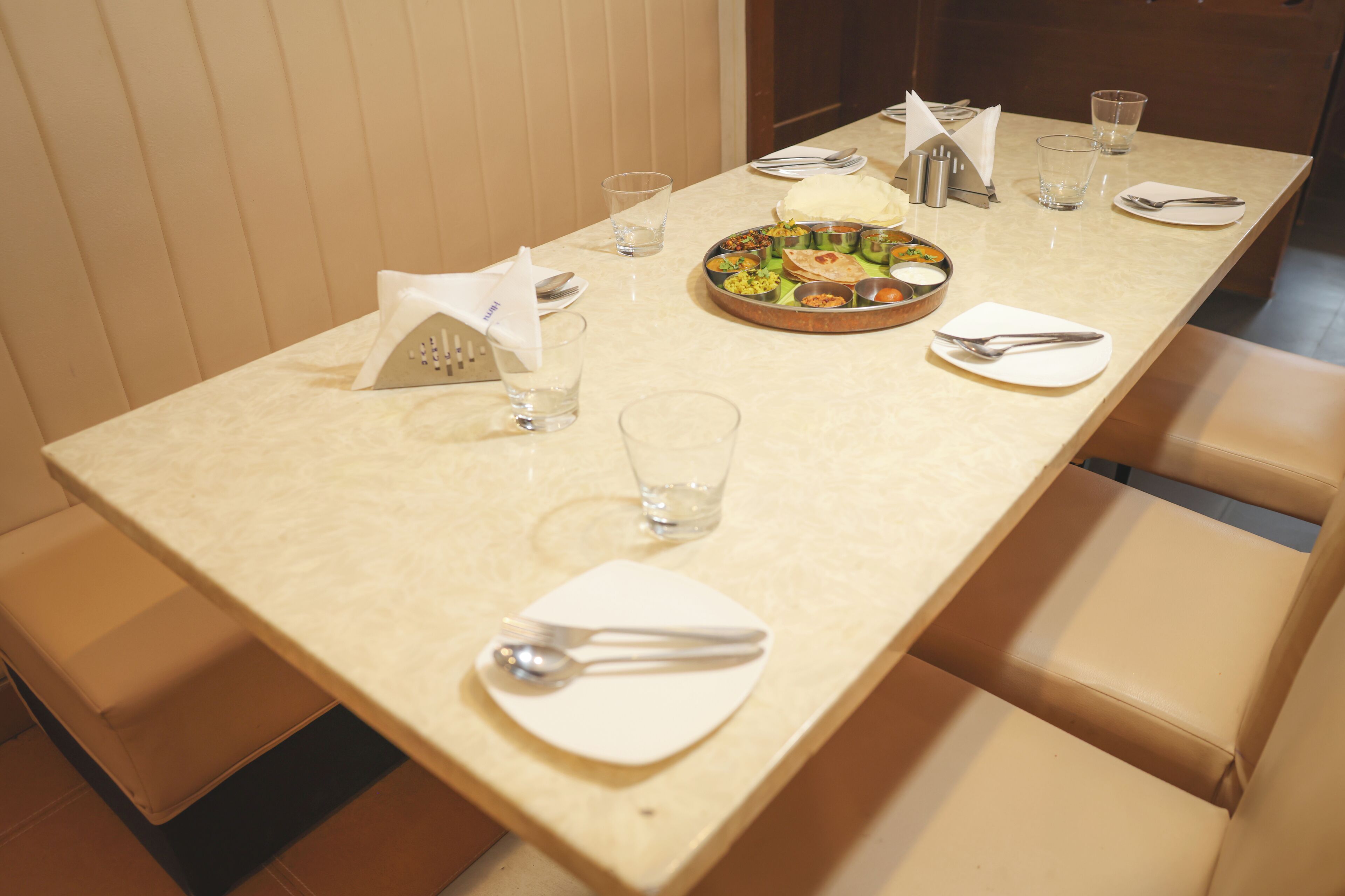 Mesa posta com pratos, talheres, copos e um prato central.