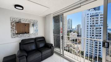 Uma sala de estar moderna com um sofá de couro preto, um espelho decorativo e vista para a cidade através de grandes janelas.