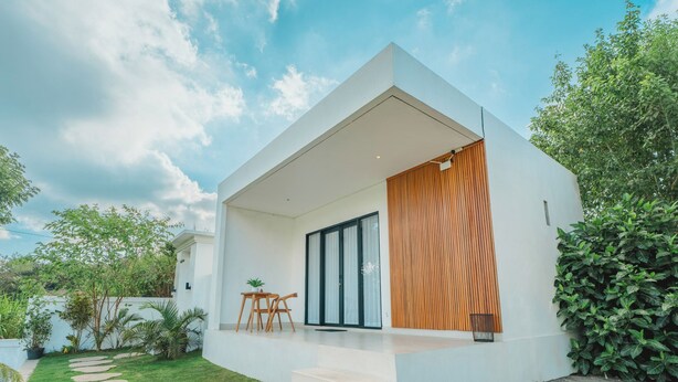 Uma casa moderna com telhado plano, parede de ripas de madeira e uma pequena área externa com mesa e cadeiras.