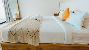 Uma cama bem arrumada com lençóis brancos, um cobertor bege e cabeceira de madeira.