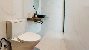 Uma casa de banho moderna com sanita, uma pia com cuba preta e um espelho na parede.