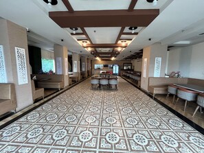 Um amplo hall de hotel com piso estampado, áreas de estar e um bar central.