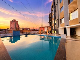 Piscina no terraço com vista desobstruída para o pôr do sol, cercada por edifícios modernos.
