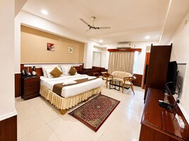 Quarto de hotel com cama, mesa de cabeceira, cadeira, televisão e ventoinha no teto.