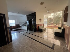 Um hall amplo com piso de mármore, escada, área de estar e grandes janelas com vista para a rua.