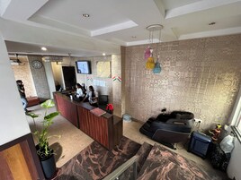 Área de recepção de hotel com balcão, televisão, decorações na parede com padrões e um espaço de estar com malas.