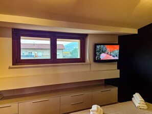 Um banheiro com janela, televisão de tela plana e uma toalha no balcão.