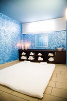 Quarto com uma cama grande, um armário de madeira escura com toalhas e uma luminária fixada na parede.