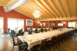Uma longa mesa de jantar posta para um evento formal em um salão com vigas de madeira e paredes vermelhas.
