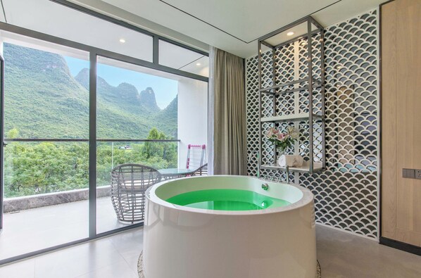 Casa de banho moderna com uma banheira grande, divisória de vidro e vista para uma paisagem montanhosa.