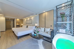 Quarto de hotel moderno com uma cama grande, um sofá, uma mesinha e uma banheira.