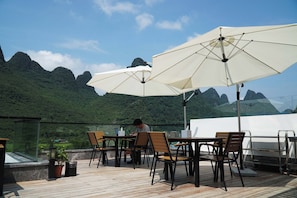 Terraço com mobiliário de exterior, guarda-sóis e vista para as montanhas.