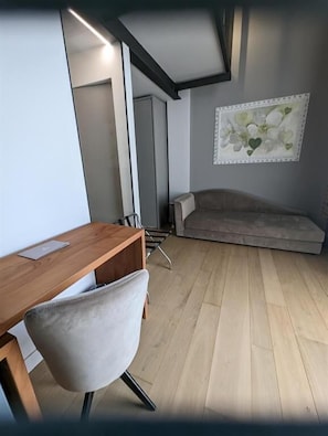 Uma sala de estar moderna com uma escrivaninha de madeira, uma cadeira cinza, um sofá e uma obra de arte na parede.