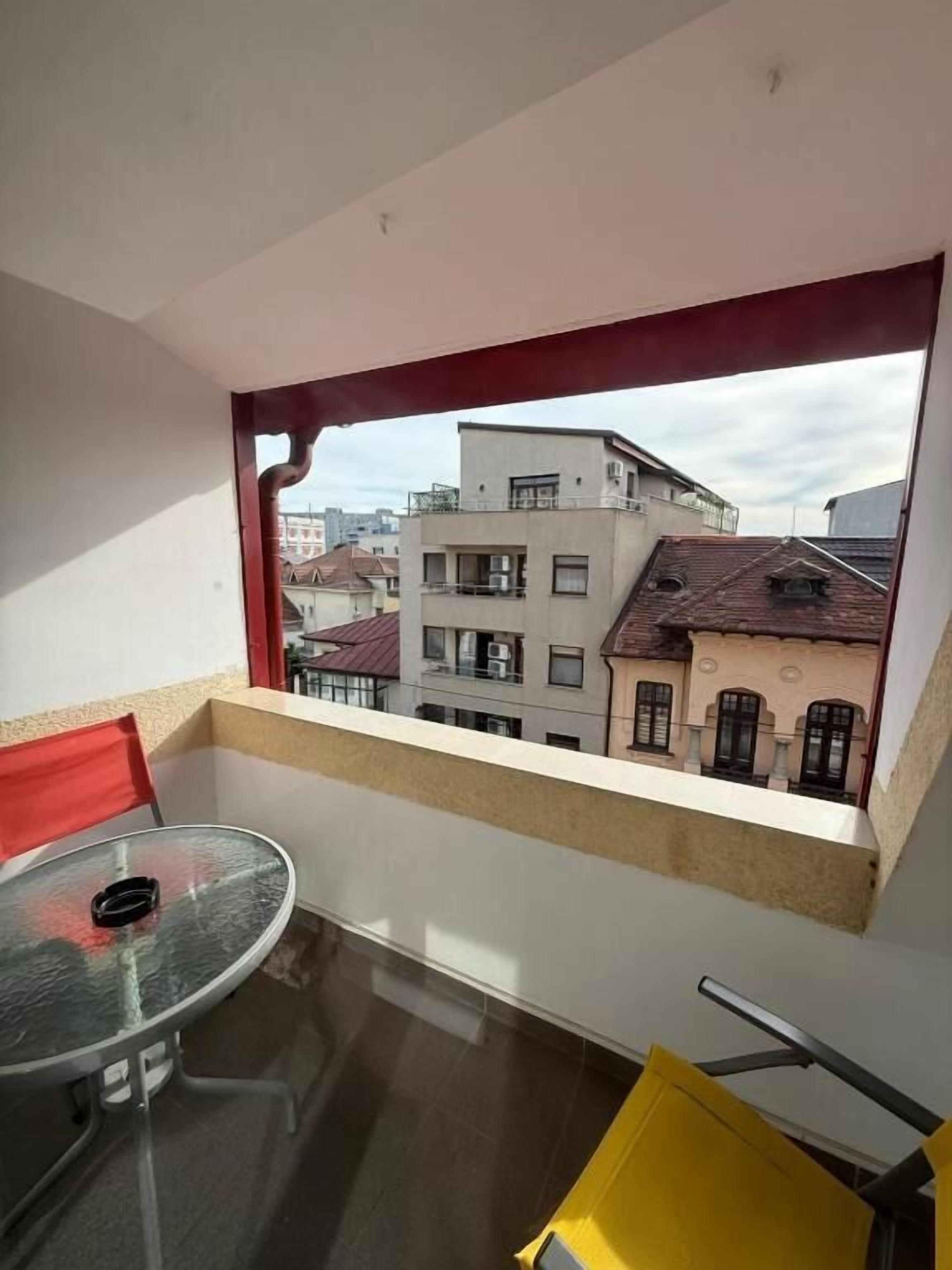 Uma varanda com mesa e cadeiras de vidro, uma cadeira vermelha e uma amarela.