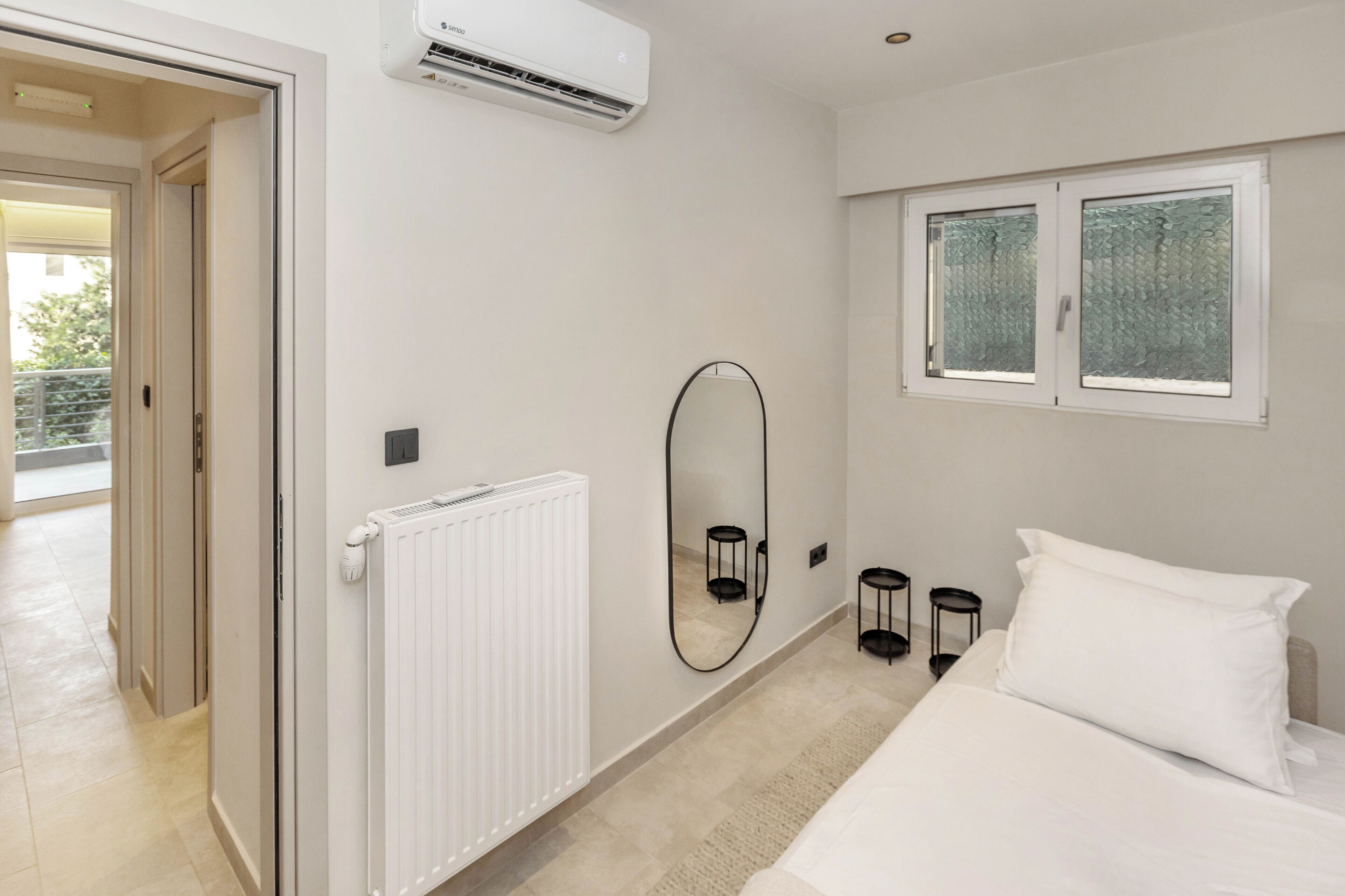 Quarto com uma cama, radiador, espelho, janela e ar condicionado.