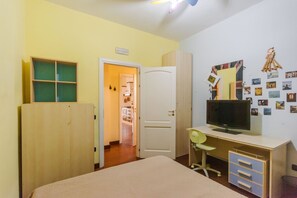 Quarto com cama, escrivaninha com computador, cadeira e guarda-roupa. Uma porta dá acesso a outro cômodo.