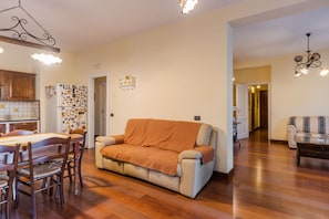 Uma sala de estar acolhedora com sofá, mesa de jantar de madeira, cadeiras e uma cozinha com armários e geladeira.