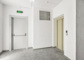 Um corredor com uma porta branca, um sinal de saída e um respiradouro na parede.