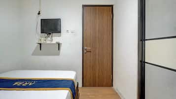 Quarto com cama, porta de madeira, televisão na parede e uma pequena prateleira.