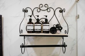 Uma prateleira no banheiro com três frascos de banho corporal e sabonete líquido para as mãos, além de um secador de cabelo.