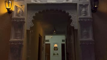 Um corredor com um arco ornamentado, um letreiro com a inscrição 'House of Bindu BNB & Homestay' e luminárias fixadas na parede.