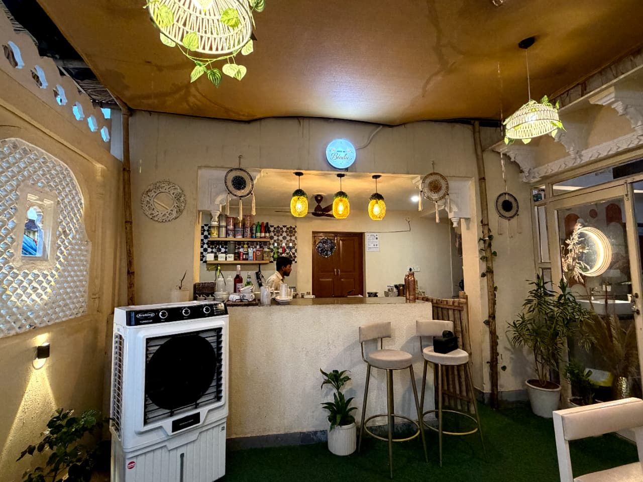Uma área de bar com balcão, banquetas, luminárias pendentes e geladeira.