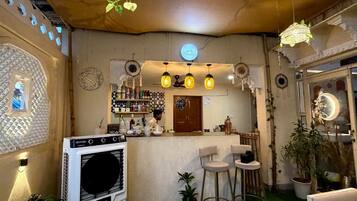 Uma área de bar com balcão, banquetas, luminárias pendentes e geladeira.