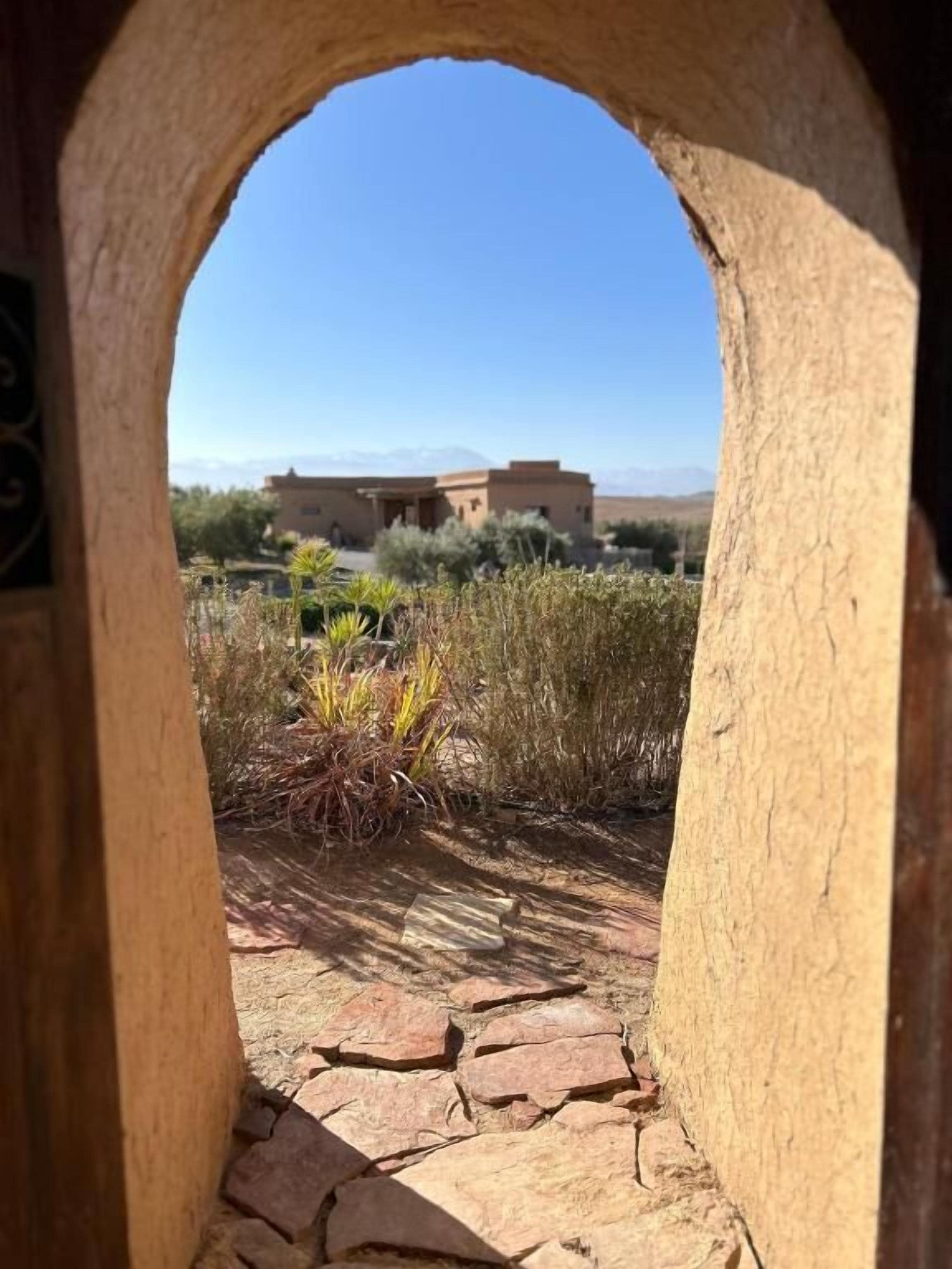 Uma porta arqueada que dá para um pátio com vista para um edifício e vegetação do deserto.