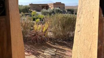 Uma porta arqueada que dá para um pátio com vista para um edifício e vegetação do deserto.