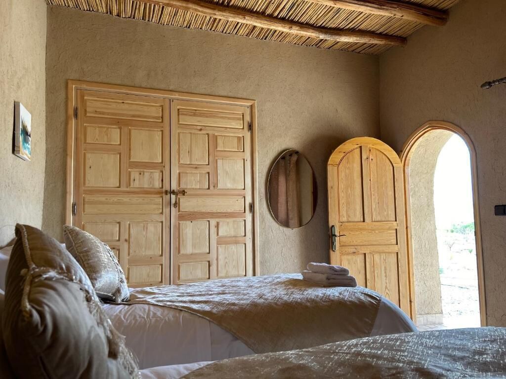 Quarto com duas camas, um guarda-roupa de madeira grande e um espelho redondo.