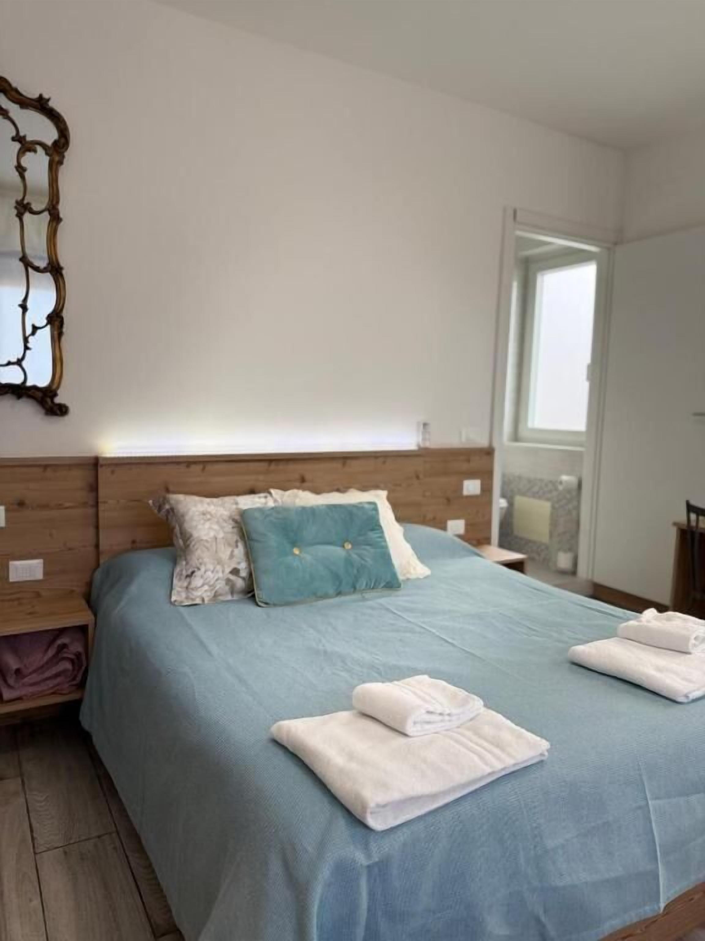Quarto com cama, almofadas, mesa de cabeceira e janela.