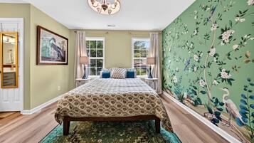 Quarto com cama, duas mesas de cabeceira, um candelabro, janela com cortinas, espelho e papel de parede floral.